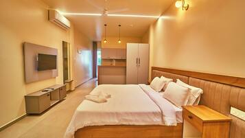 Quarto de hotel com cama, mesa de cabeceira e televisão fixada na parede.