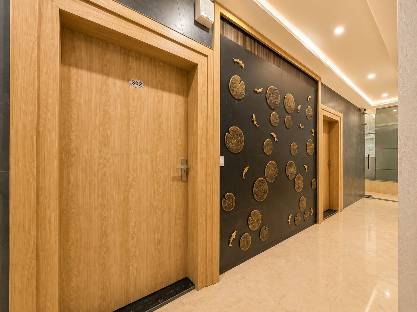 Corredor com portas de madeira, numeradas 302, e uma parede com desenhos circulares.