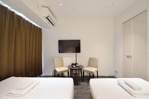 Quarto de hotel com duas camas, televisão e mesa com cadeiras.