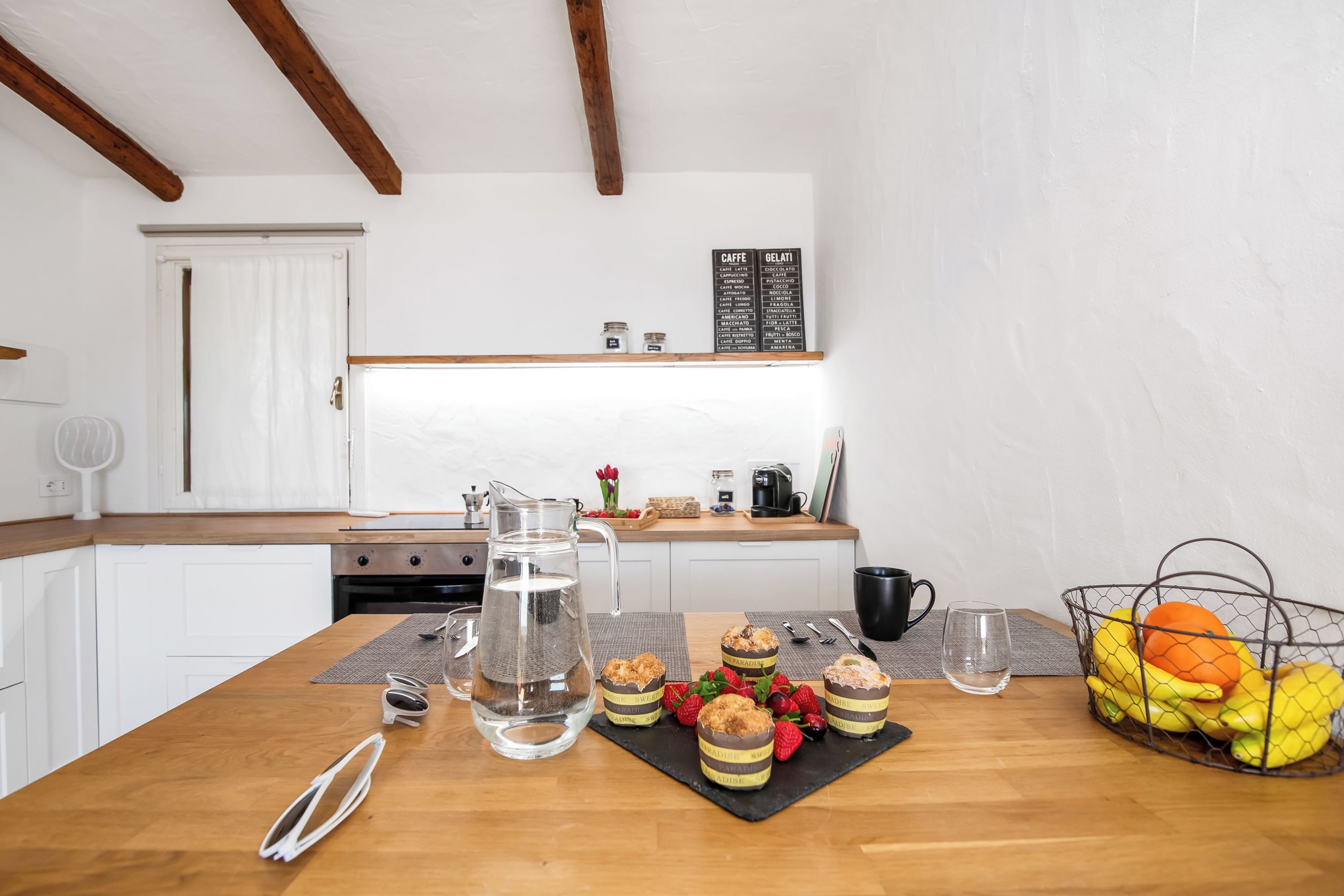 Uma cozinha com mesa de madeira, cardápio de café e cesta de frutas.