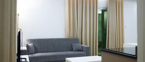Uma sala de estar moderna com um sofá cinzento, uma mesa de centro branca e cortinas bege.