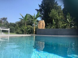 Piscina transparente com vista para vegetação e uma grande estrutura rochosa.