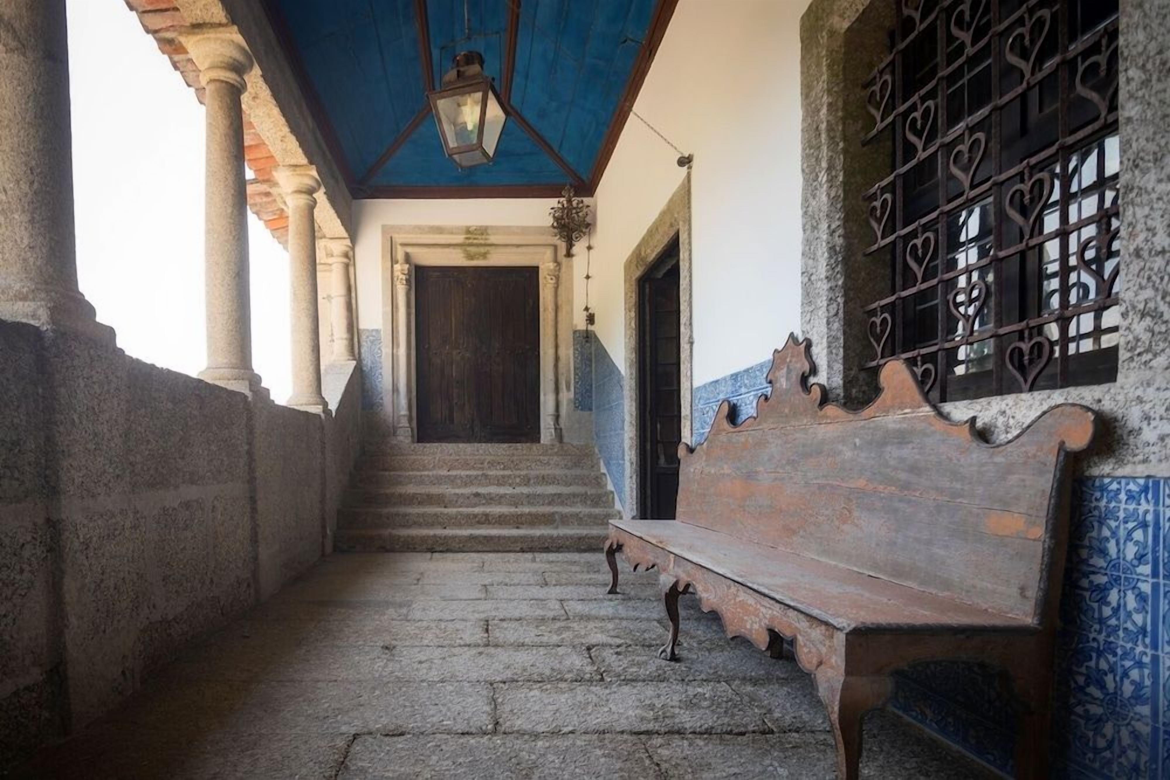 Corredor com um banco de madeira, escada e parede com grades de janela em formato de coração.