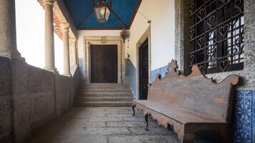Corredor com um banco de madeira, escada e parede com grades de janela em formato de coração.