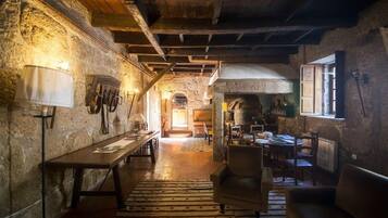 Interior rústico com paredes de pedra, teto de madeira, área de jantar com cadeiras e mesa, e um tapete estampado.