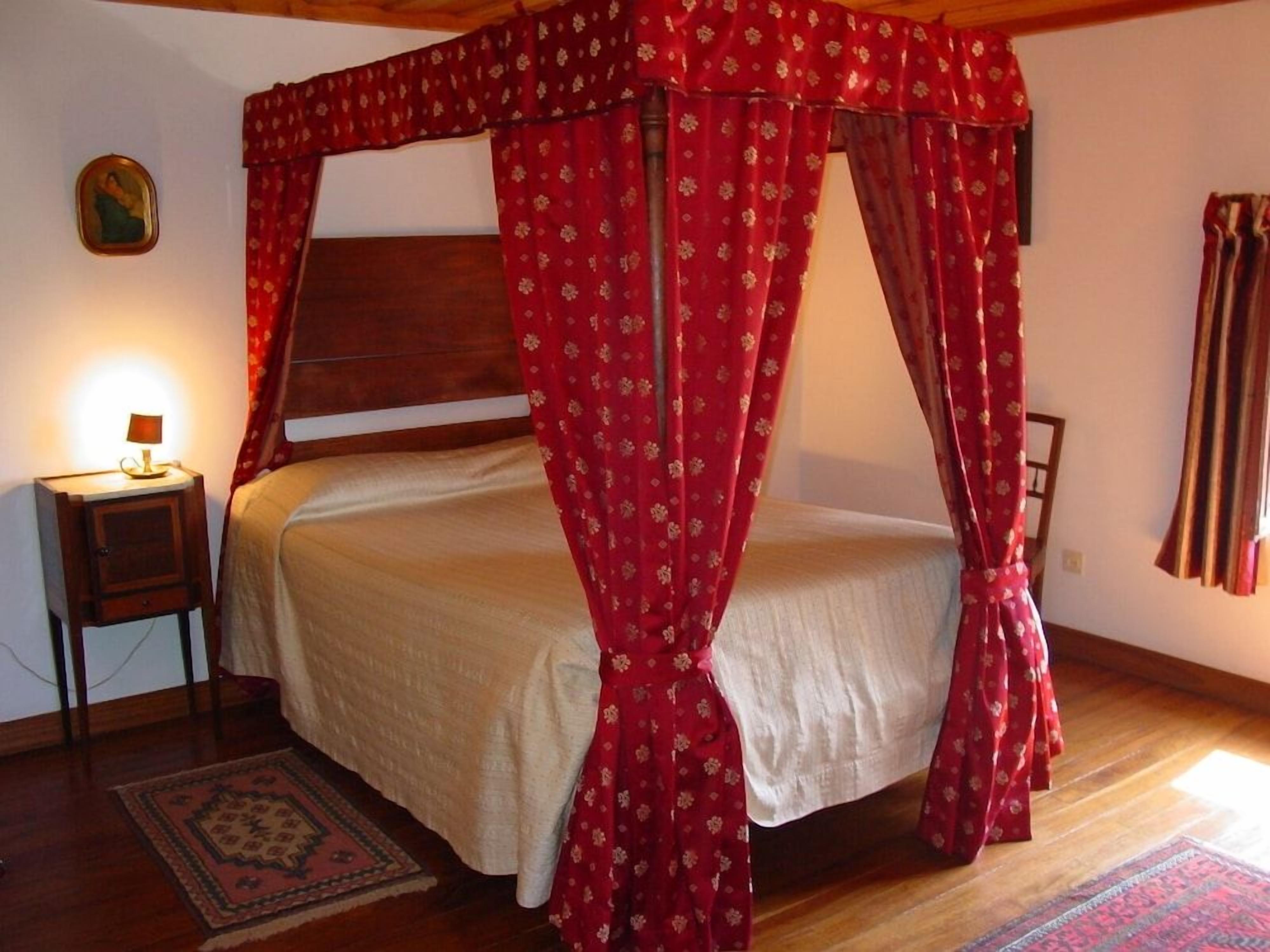 Quarto com cama de dossel, mesa de cabeceira, abajur e tapete.