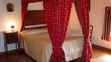 Quarto com cama de dossel, mesa de cabeceira, abajur e tapete.