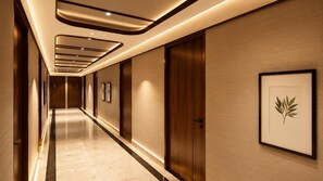 Corredor de hotel com portas de madeira, obras de arte emolduradas e iluminação embutida.
