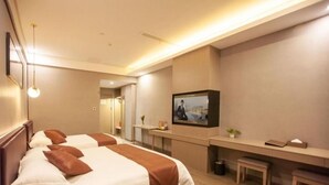 Quarto de hotel com duas camas, uma escrivaninha, televisão e um pequeno espaço de estar.