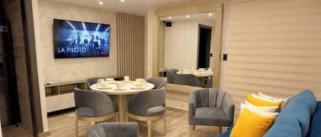 Uma sala de estar moderna com uma televisão, uma mesa de jantar com cadeiras e um sofá com almofadas.