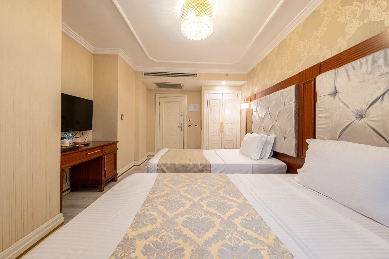 Quarto de hotel com duas camas, uma mesa de trabalho e uma televisão, além de um tapete estampado.
