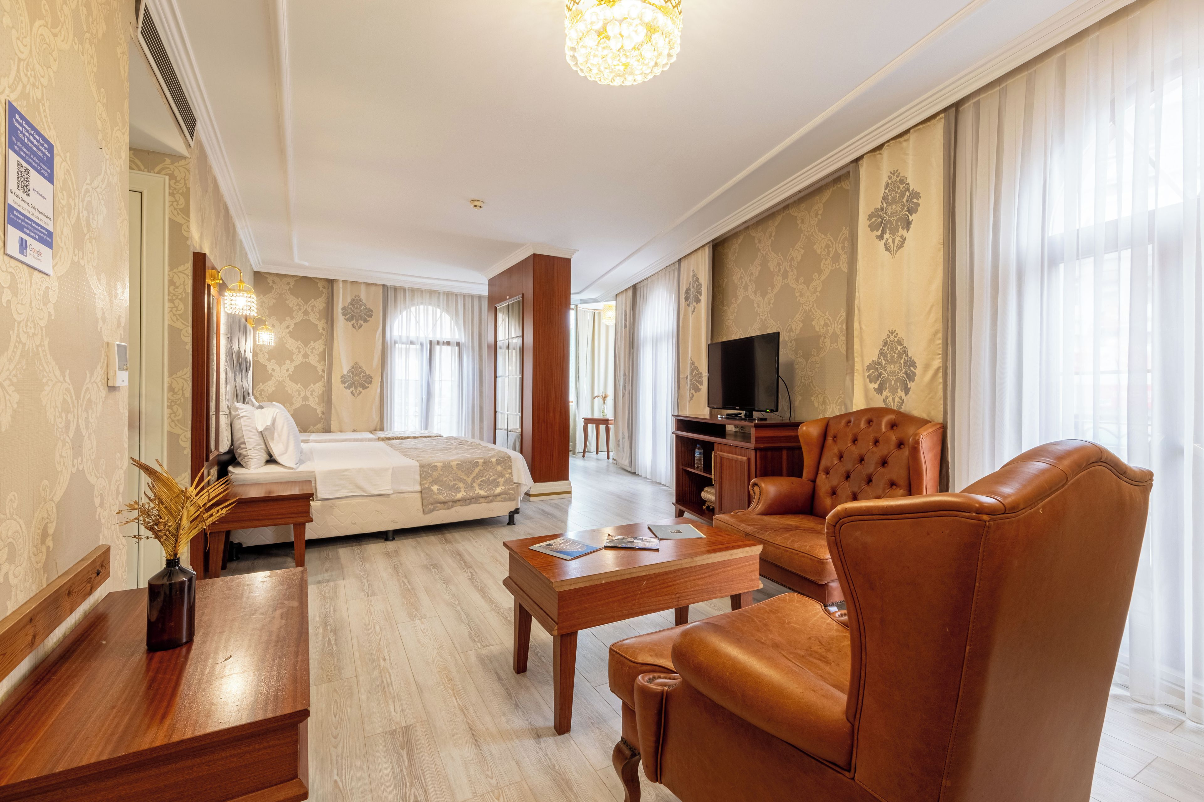 Quarto de hotel com uma cama, um sofá, uma mesa de centro, uma televisão e um vaso decorativo.