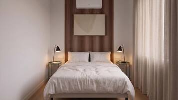 Quarto moderno com cama, duas mesas de cabeceira com luminárias, ar-condicionado fixado na parede e uma janela grande com cortinas.