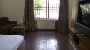 Quarto de hotel com cama, televisão, sofá, mesa pequena e janela com cortinas.