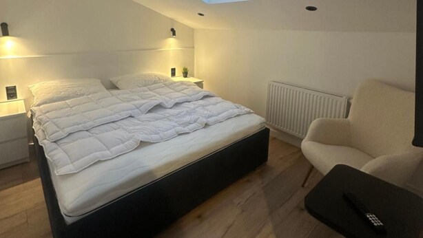 Quarto moderno com claraboia, uma cama, abajures, radiador e uma cadeira.