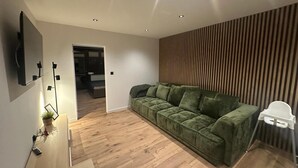 Uma sala de estar moderna com um sofá verde, piso de madeira e uma TV fixada na parede.
