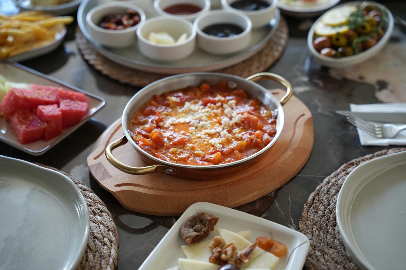 Mesa de jantar com diversos pratos, incluindo uma tigela de sopa, uma fatia de melancia e vários pequenos recipientes com acompanhamentos.