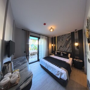 Quarto de hotel moderno com uma cama grande, televisão de tela plana, mesa de cabeceira de mármore e porta de vidro deslizante para o exterior.
