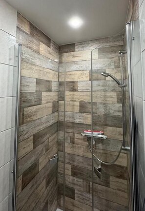 Chuveiro com porta de vidro, chuveiro de metal e parede com textura que imita madeira.
