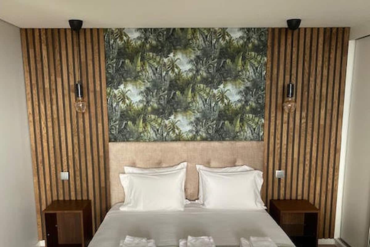 Quarto com uma cama grande, duas mesas de cabeceira, uma cadeira verde e uma parede com ripas de madeira verticais.