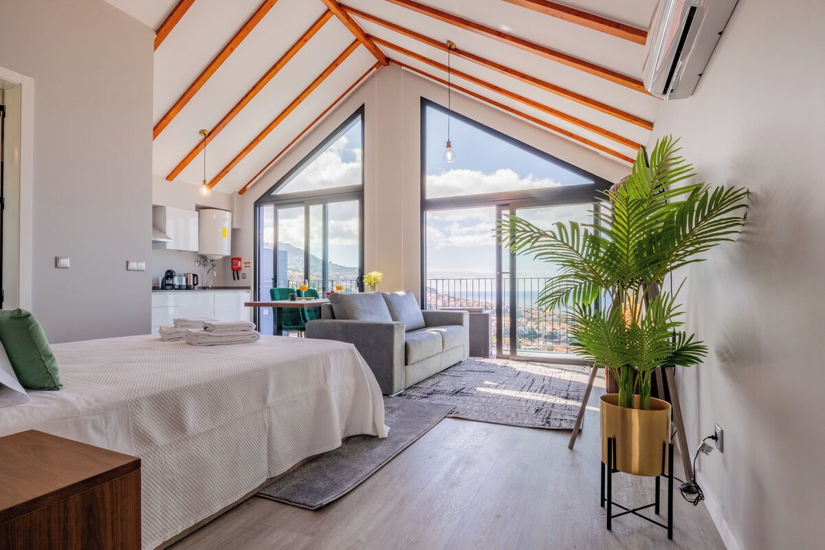 Quarto moderno com uma cama grande, varanda com vista e área de cozinha.