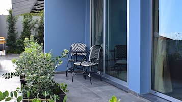 Uma área de estar moderna ao ar livre, com parede azul, grandes portas de vidro deslizantes e plantas em vasos.