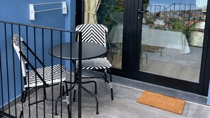 Uma varanda com mesa e cadeiras, vista para o mar e um edifício com fachada amarela.