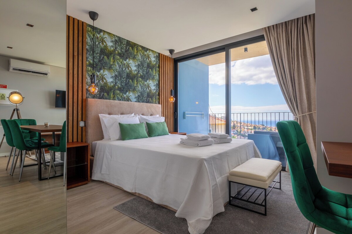 Quarto de hotel com cama, mesa de jantar, cadeiras, vista para o mar e uma grande janela.