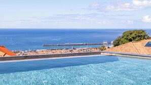 Piscina azul e límpida com vista para o mar e um cais distante.