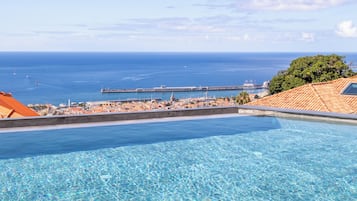 Piscina azul e límpida com vista para o mar e um cais distante.