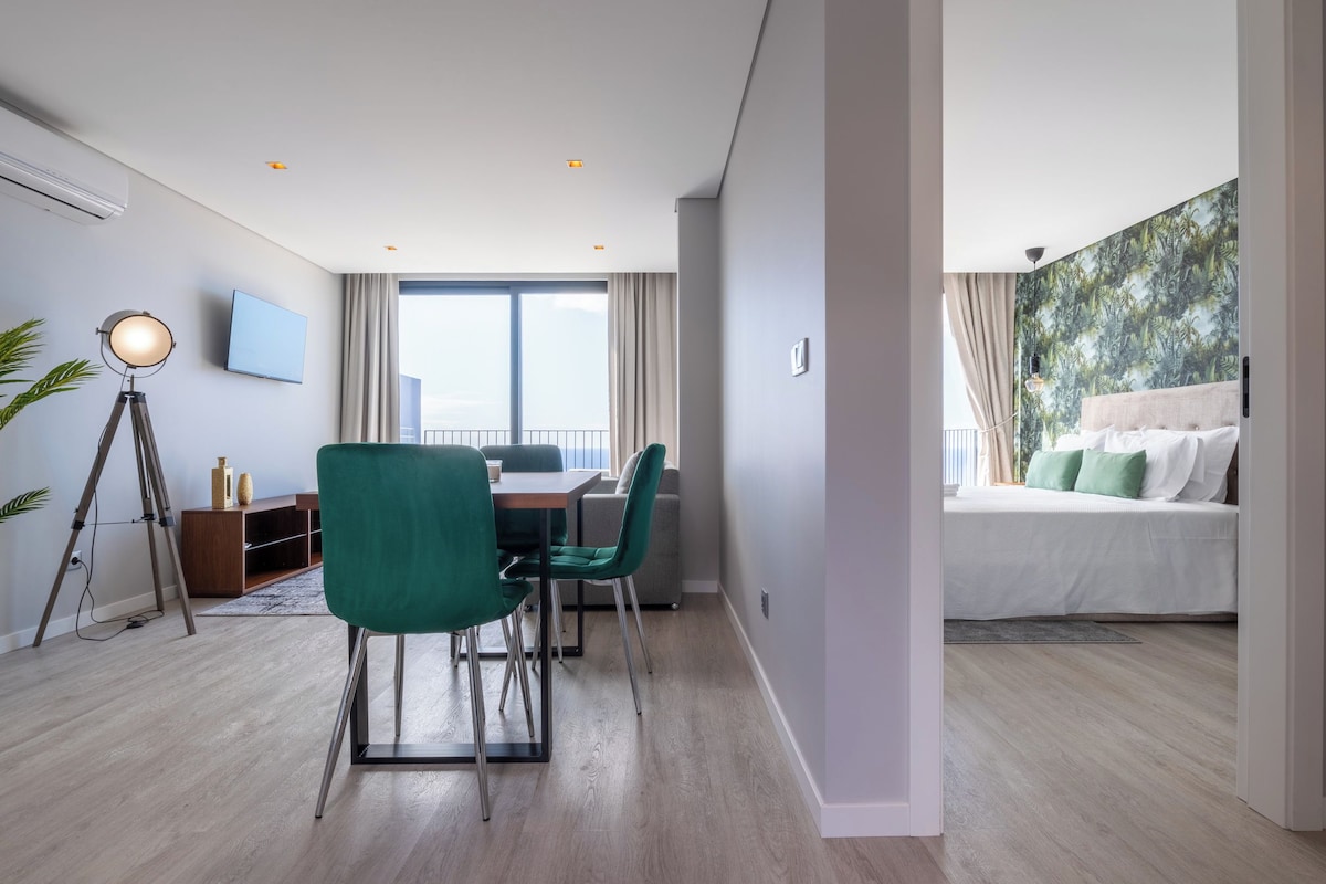 Quarto de hotel moderno com varanda, área de refeições e cama com vista.