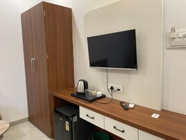 Quarto com guarda-roupa de madeira, televisão de tela plana na parede, frigorífico pequeno, máquina de café e comando remoto sobre a bancada.