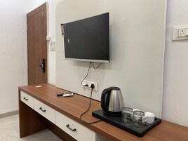 Quarto de hotel com secretária de madeira, televisão de tela plana na parede, chaleira e bandeja com copos e xícara.