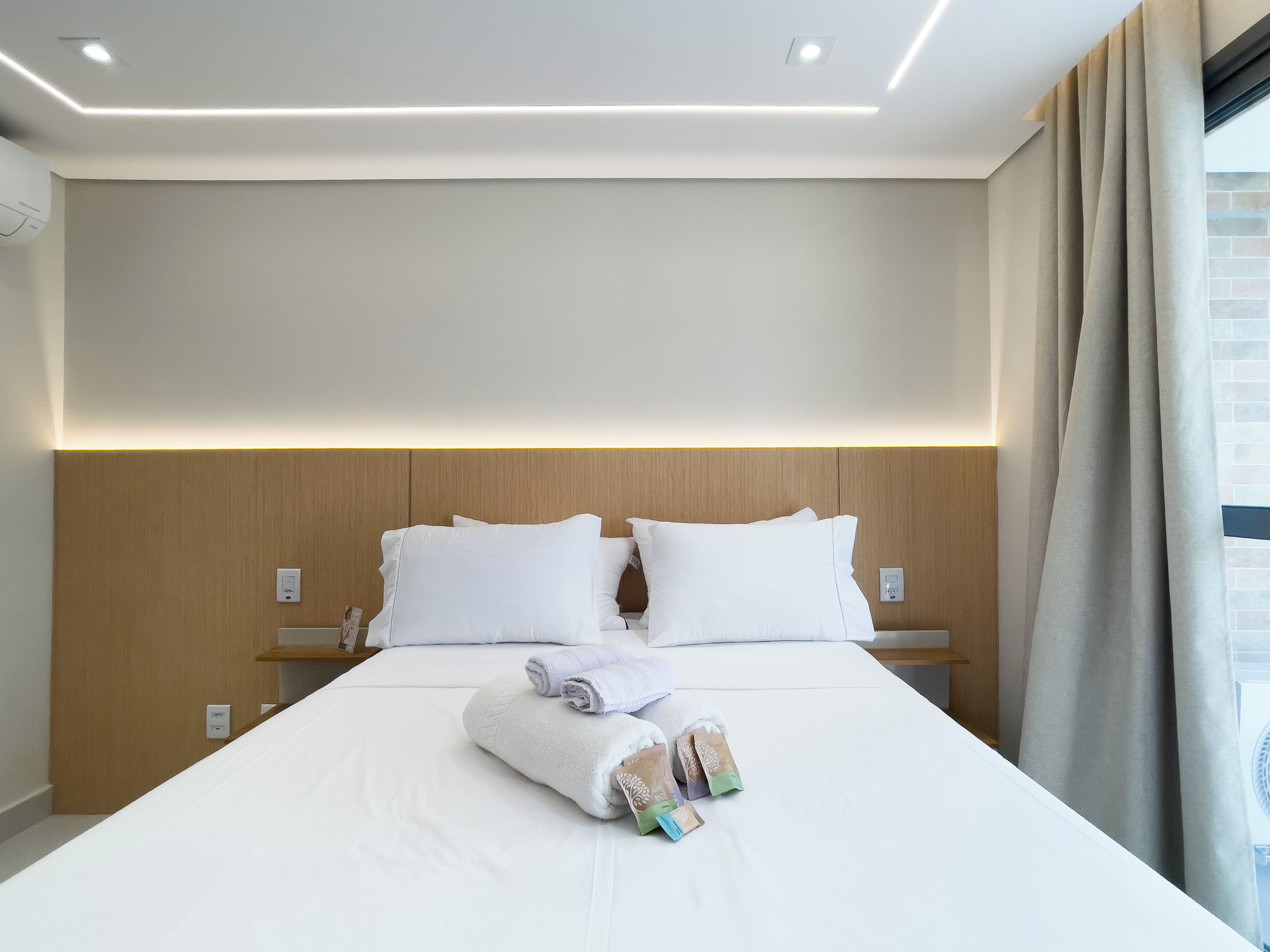 Quarto de hotel com uma cama grande, duas mesas de cabeceira e cabeceira com iluminação integrada.