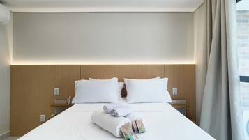 Quarto de hotel com uma cama grande, duas mesas de cabeceira e cabeceira com iluminação integrada.