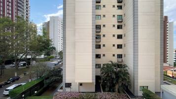 Edifício residencial com vários andares, varandas, área de estacionamento e um pequeno jardim com flores.