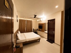 Quarto de hotel com cama, escrivaninha, espelho, ventoinha no teto e porta.