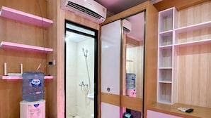 Casa de banho moderna com chuveiro, sanita e lavatório. Inclui um dispensador de água, um banquinho rosa e uma área de secretária com iluminação rosa.