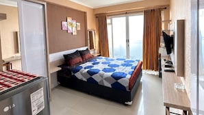 Quarto de hotel com cama, escrivaninha, geladeira e vista para o exterior.