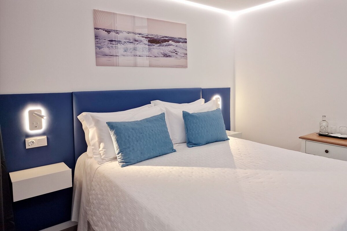 Quarto moderno com cama, mesas de cabeceira e luminária fixada na parede.