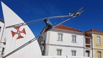 Um veleiro com o emblema de uma cruz vermelha, atracado perto de edifícios com telhado em tijolos vermelhos.