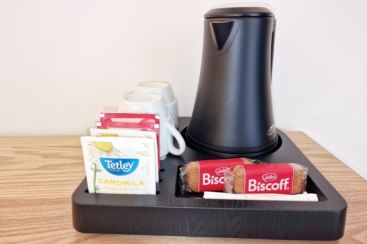 Uma bandeja com cafeteira, sachês de chá, biscoitos e leite condensado.