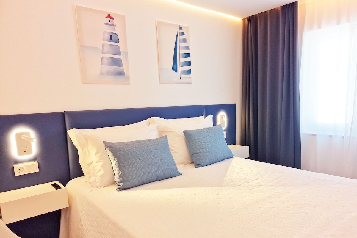 Quarto de hotel com cama, mesas de cabeceira, poltrona e obras de arte na parede.