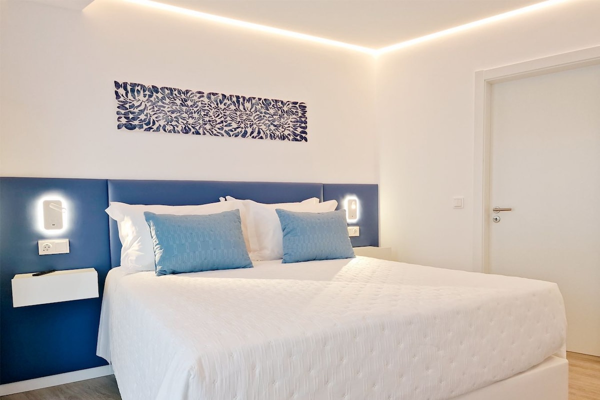 Quarto moderno com uma cama grande, mesas de cabeceira e luminária na parede.