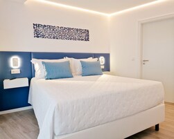 Quarto moderno com uma cama grande, mesas de cabeceira e luminária na parede.