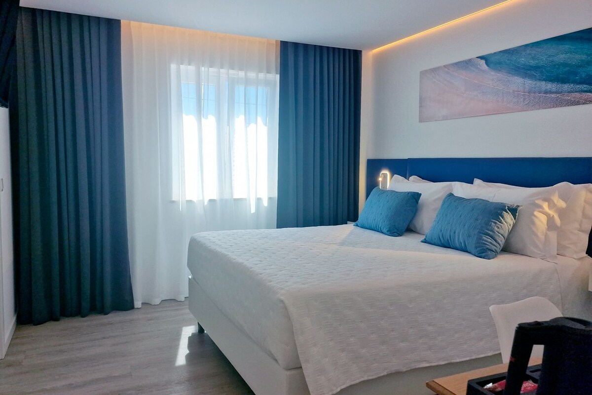 Quarto de hotel moderno com uma cama grande, cortinas azuis e um quadro na parede.