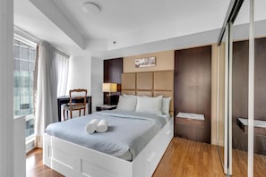 Quarto de hotel moderno com cama grande, escrivaninha, cadeira, mesa de cabeceira e janela com cortinas.