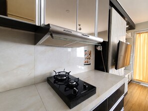 Cozinha com fogão preto, coifa de aço inoxidável e televisão na parede.
