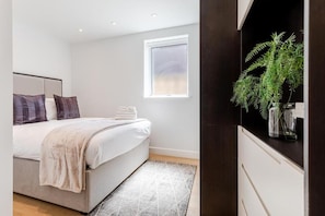 Quarto com cama, almofadas, mesa de cabeceira, janela e planta.