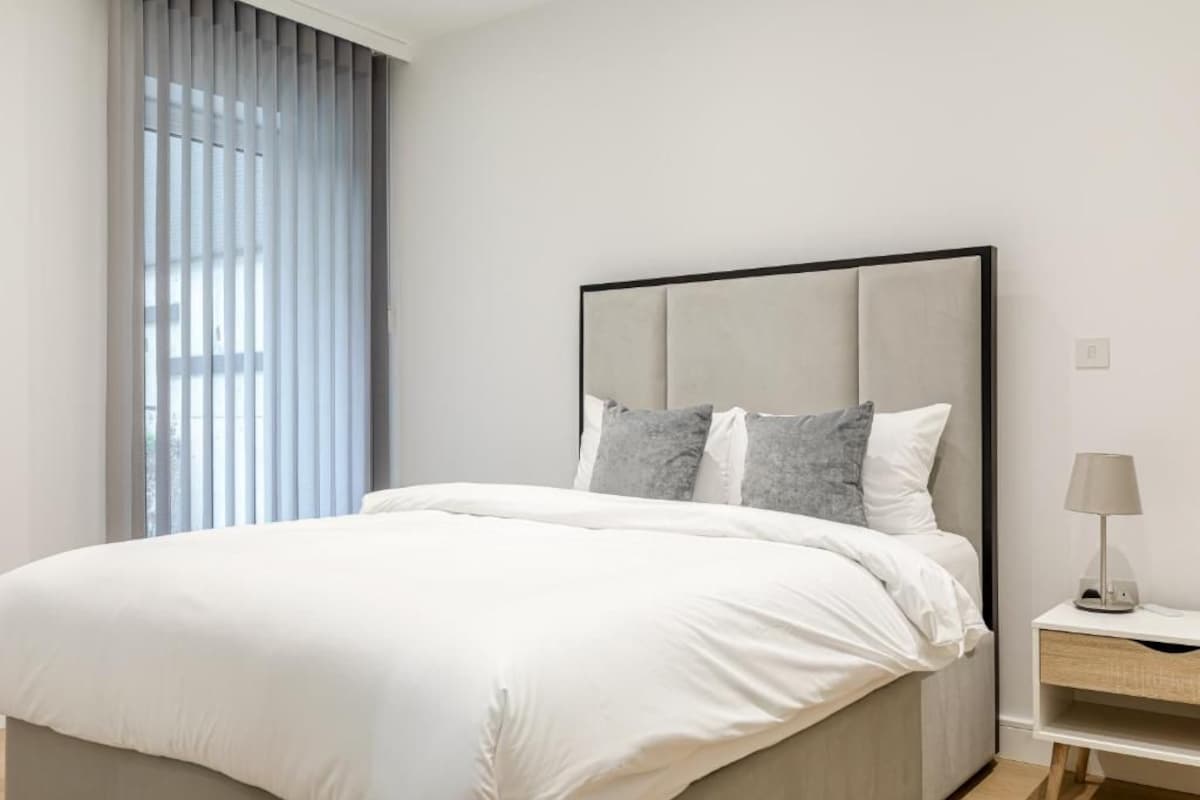 Quarto moderno com cama, mesa de cabeceira e janela com persianas.